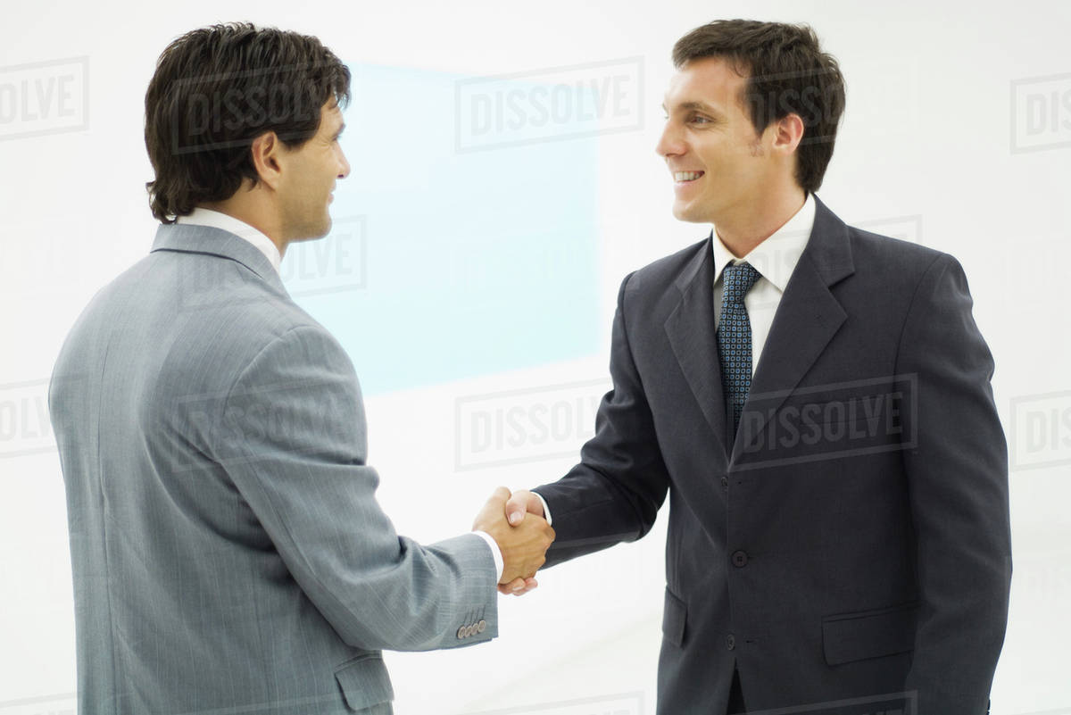 Two businessmen shaking hands, smiling at each other, side view ...