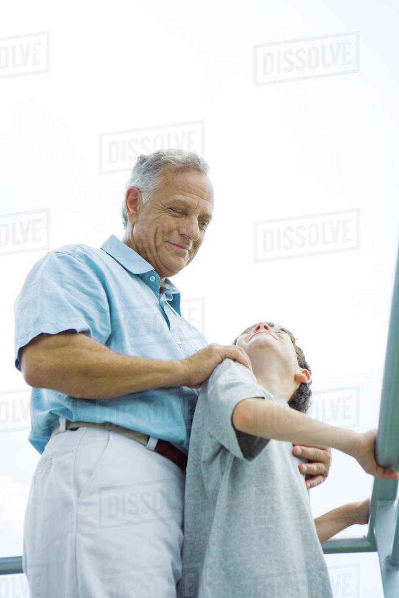 Grandfather and grandson standing by railing together, smiling at each ...