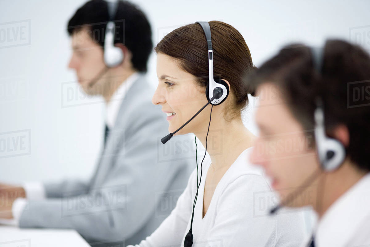 Call center, focus on woman wearing headset, smiling, side view ...