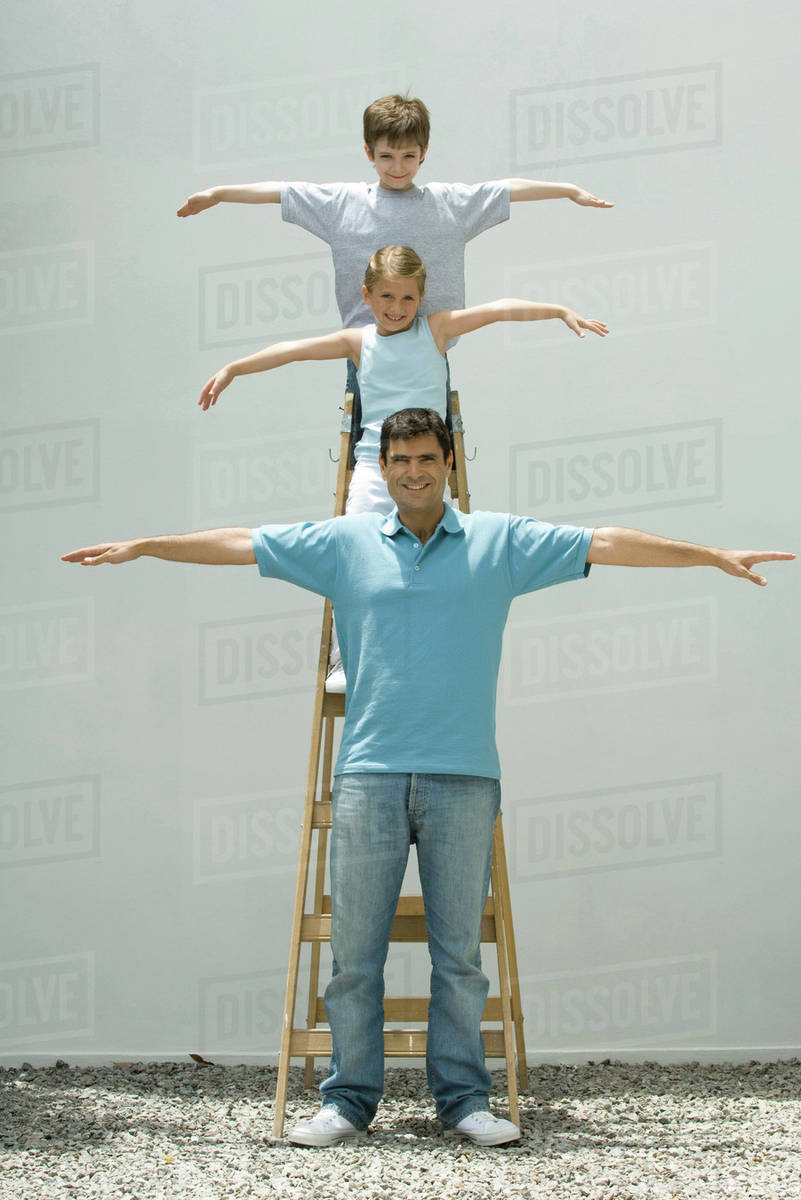 Boy and girl standing on ladder with arms in the air, father standing ...