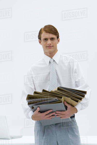 Professional man carrying a disorganized stack of binders, looking at ...