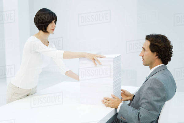 Professional woman and businessman exchanging tall stack of paper ...