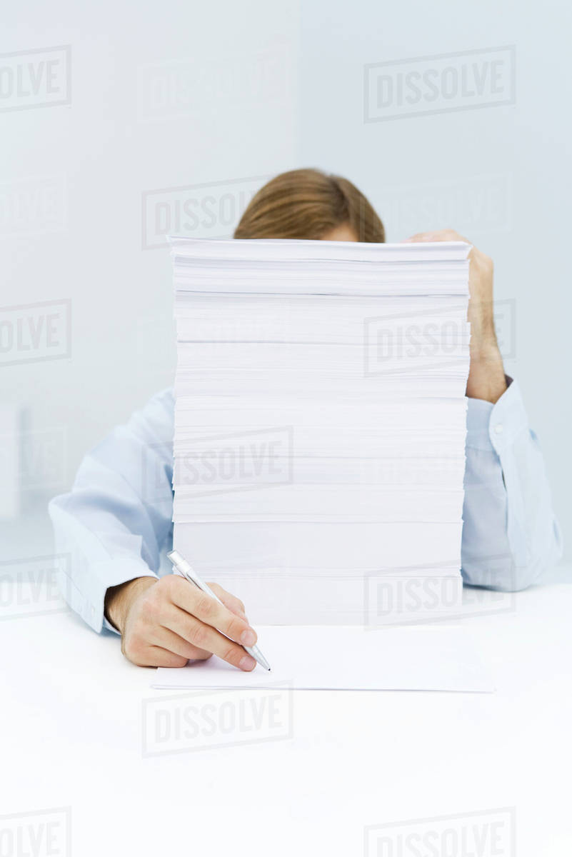 Man hiding behind tall stack of paper, reaching around to write on a ...
