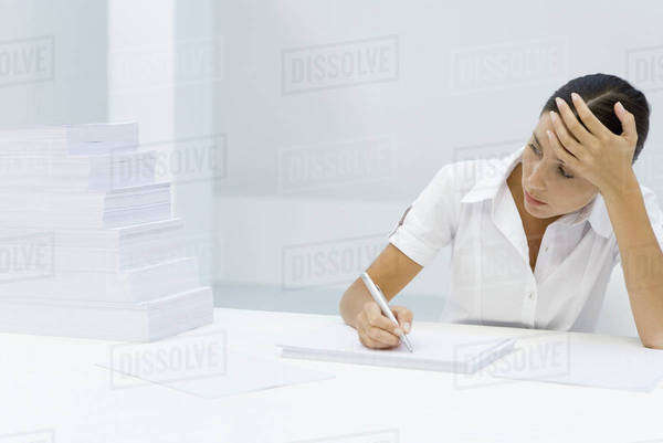 Woman holding her forehead, writing on blank sheet of paper, looking at ...