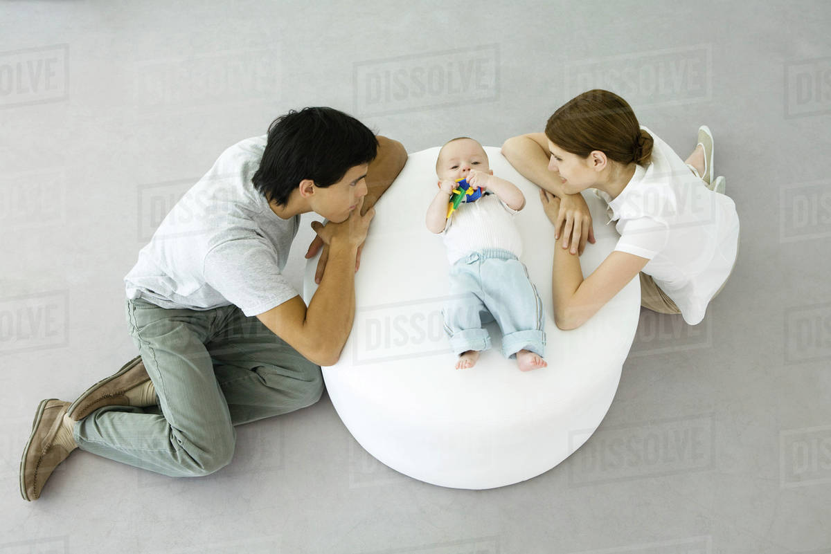 Young parents leaning against ottoman, looking at baby lying between ...