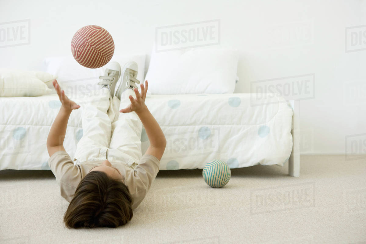 Boy lying on the ground in bedroom, throwing ball in the air - Royalty ...