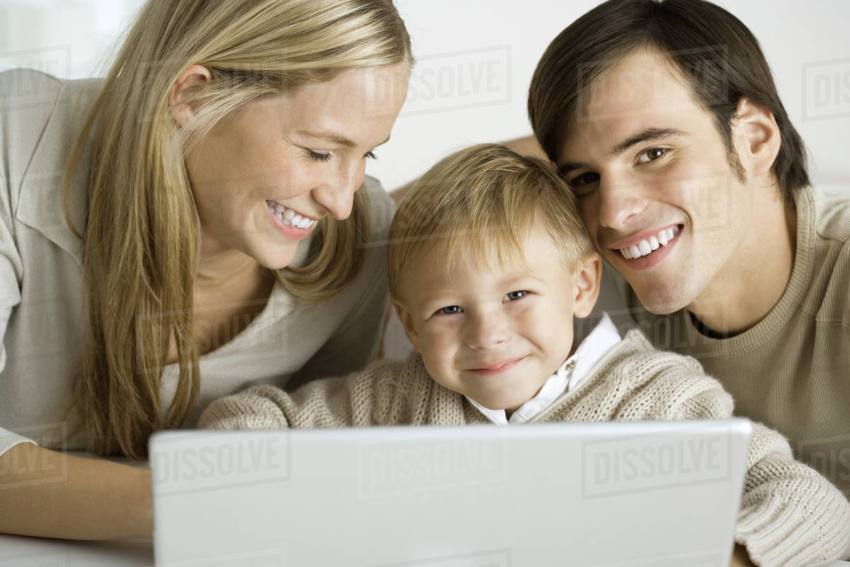 Family gathered around laptop computer, father and son smiling at ...