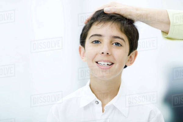 Adult's hand on child's head, boy smiling at camera, cropped view ...