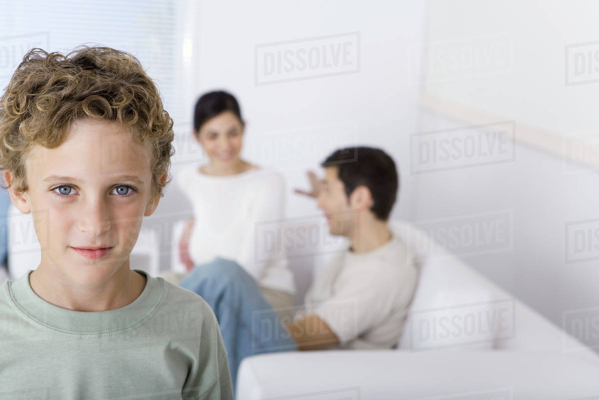 Boy smiling at camera, parents chatting in background - Stock Photo ...