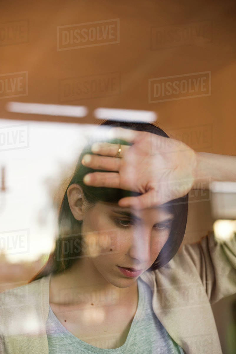 Woman leaning against window looking down - Stock Photo - Dissolve