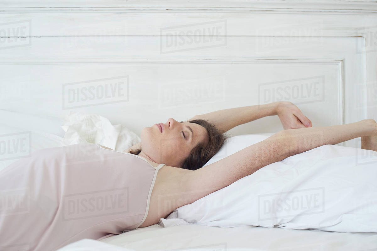 Woman lying on back in bed stretching - Royalty-free Stock Photo | Dissolve