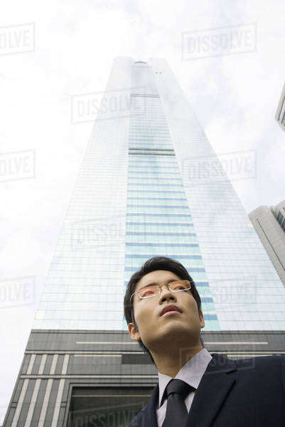Young businessman standing in front of skyscraper, low angle view ...
