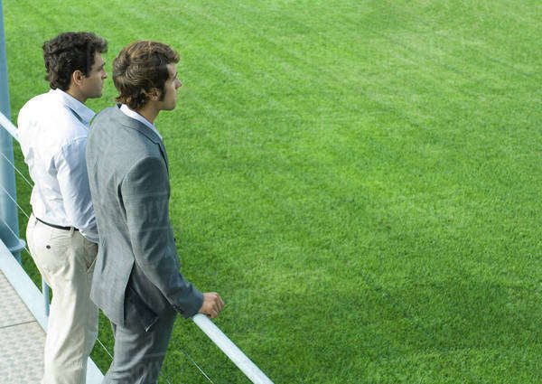 Two businessmen standing on walkway, looking into distance - Stock ...