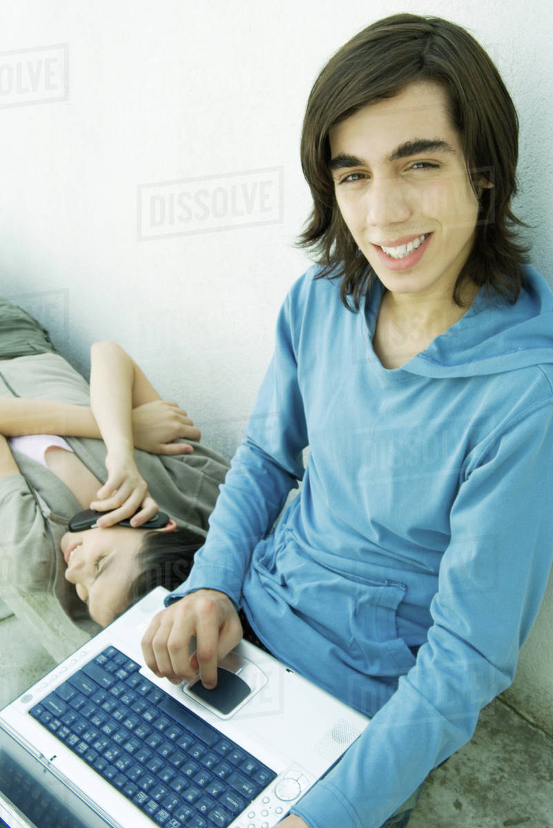 Teen boy using laptop while female friend uses cell phone - Royalty ...