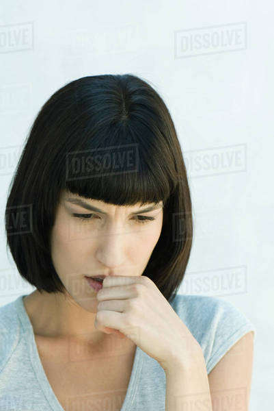 Woman biting thumb and looking down, head and shoulders, portrait ...