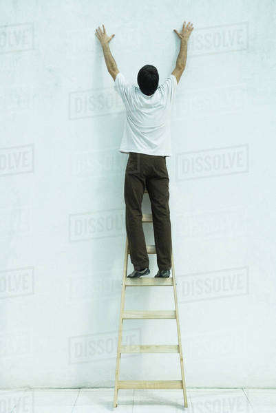Man standing on ladder, reaching up along wall, full length - Royalty ...