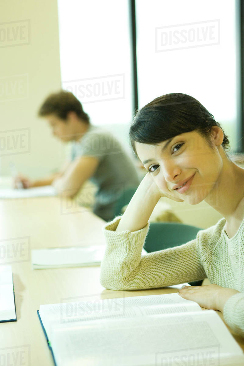 Female college student sitting at table with book, smiling at camera ...