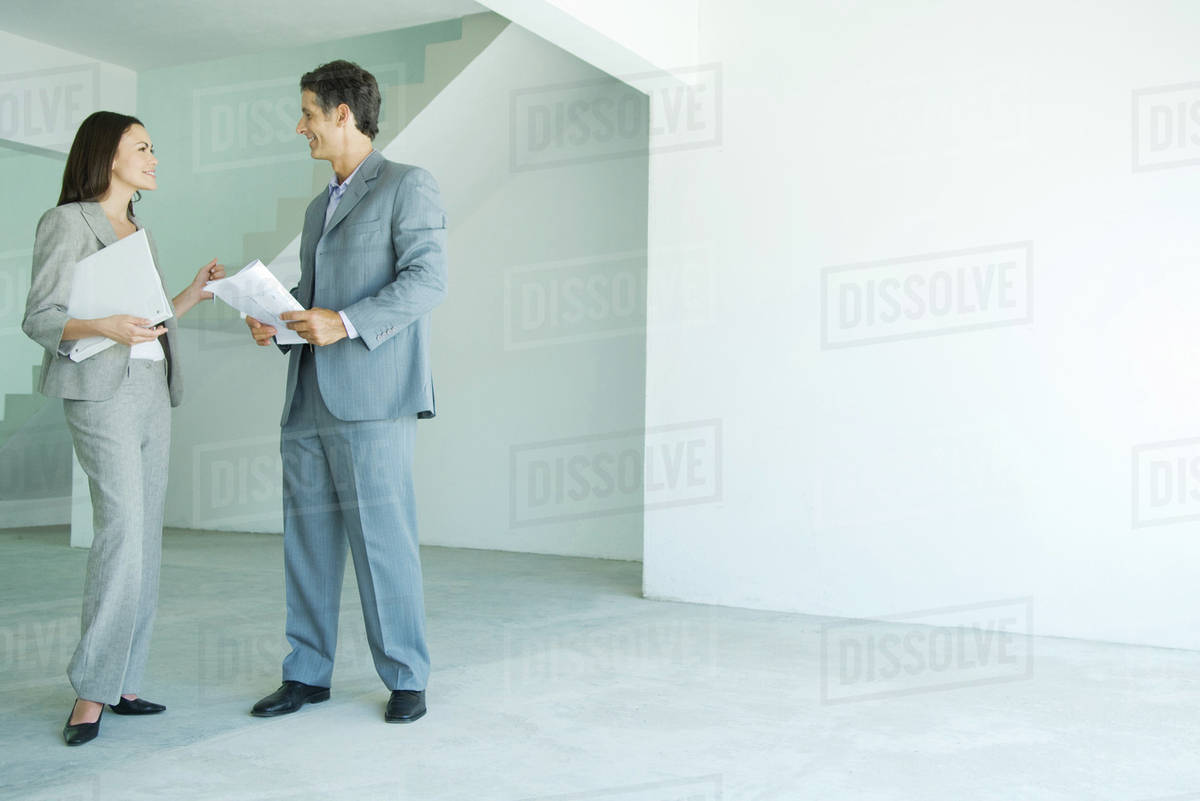 Man and woman in suits standing in empty home interior, smiling, face ...