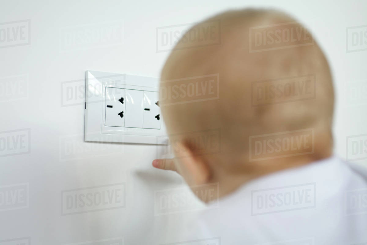 Baby touching electric outlet, rear view - Stock Photo - Dissolve