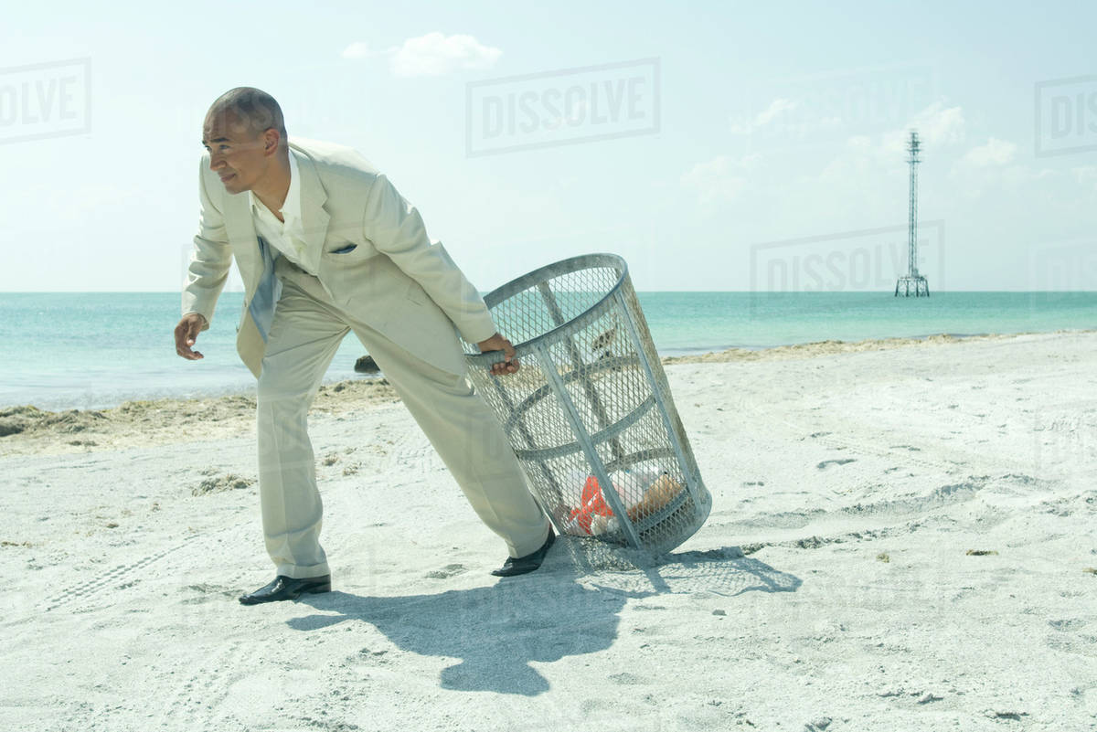 Man in suit pulling garbage can across sunny beach, full length - Stock ...