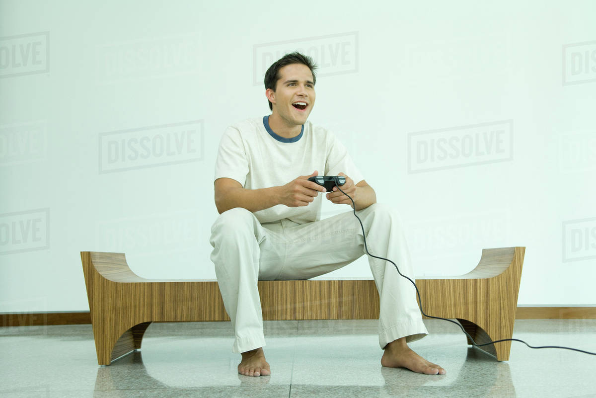 Young man playing video game, smiling - Royalty-free Stock Photo | Dissolve