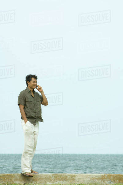 Man standing using cell phone, ocean in background - Stock Photo - Dissolve