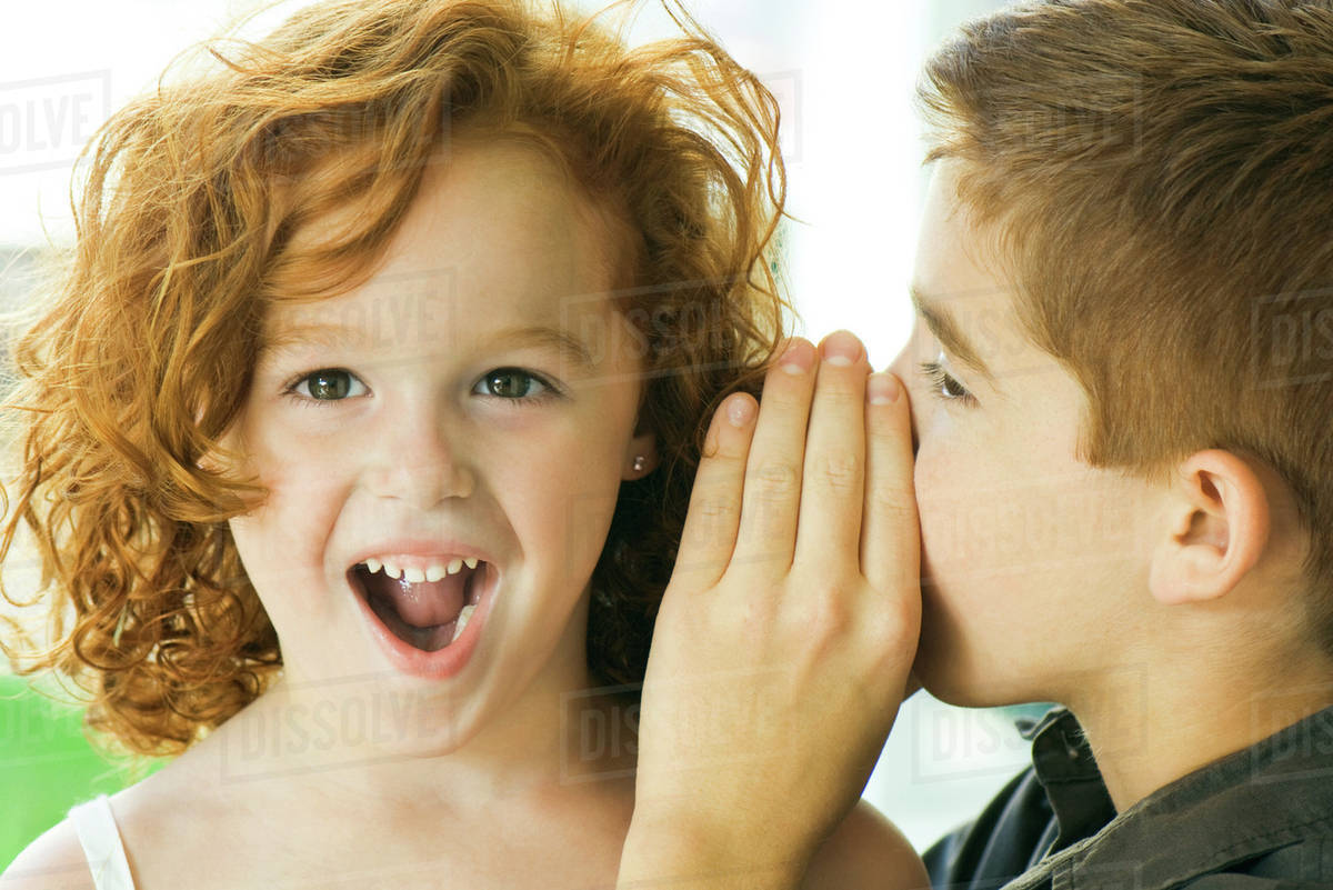 Boy whispering in girl's ear, close-up - Stock Photo - Dissolve