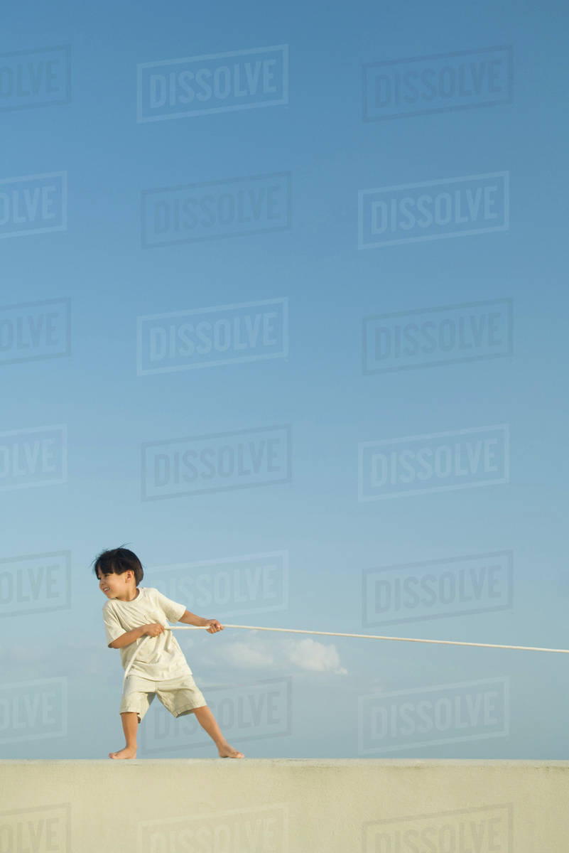 Little boy pulling on rope, blue sky in background, full length ...