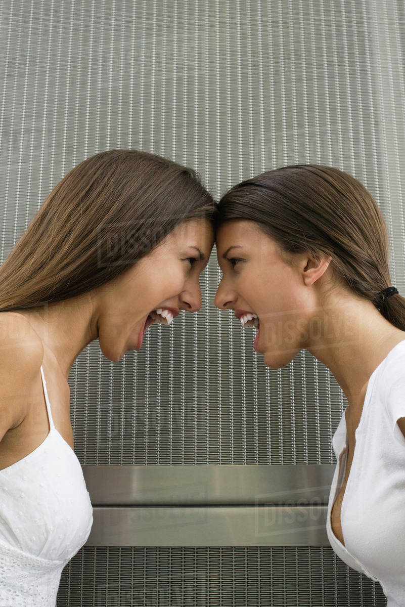Twin sisters face to face, touching foreheads, mouths open, side view ...