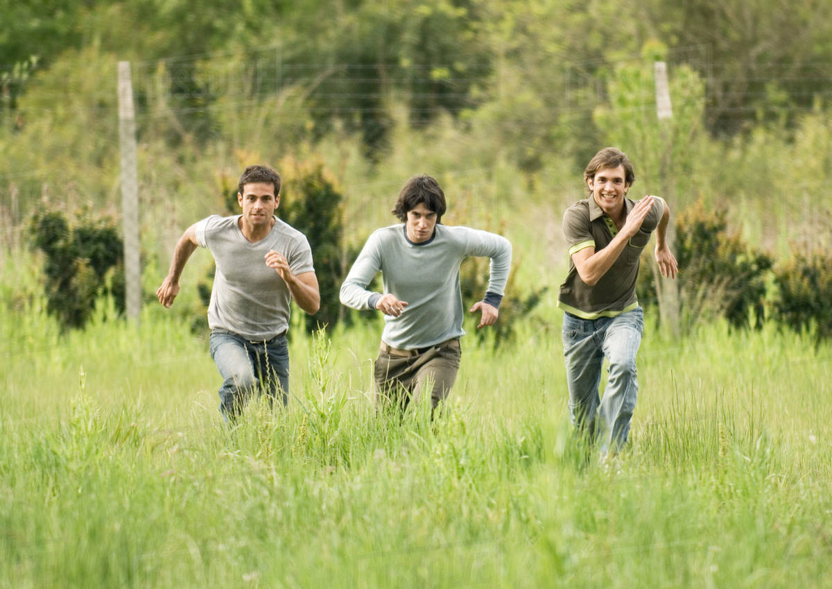 Three young male friends racing across field - Royalty-free Stock Photo ...