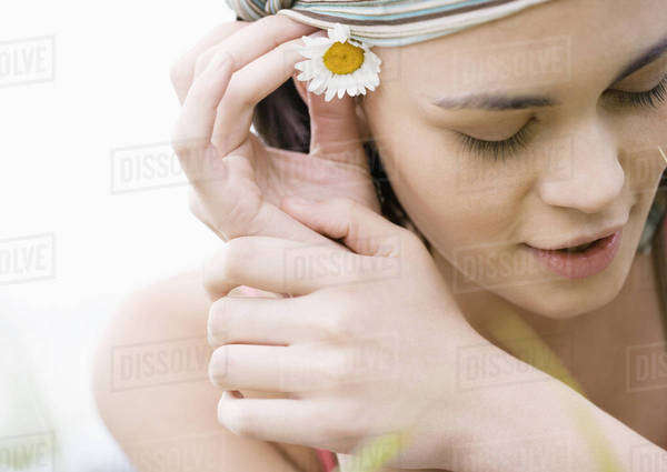 Young woman putting flower behind ear - Royalty-free Stock Photo | Dissolve