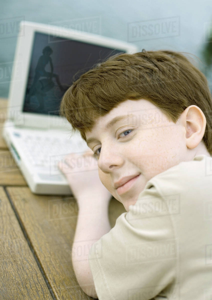 Boy using laptop, looking over shoulder at camera - Royalty-free Stock ...