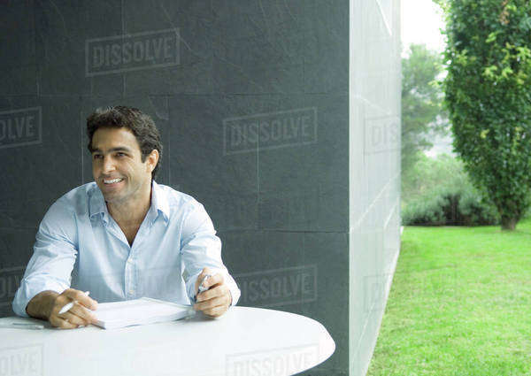 Man sitting at table outdoors, working - Stock Photo - Dissolve