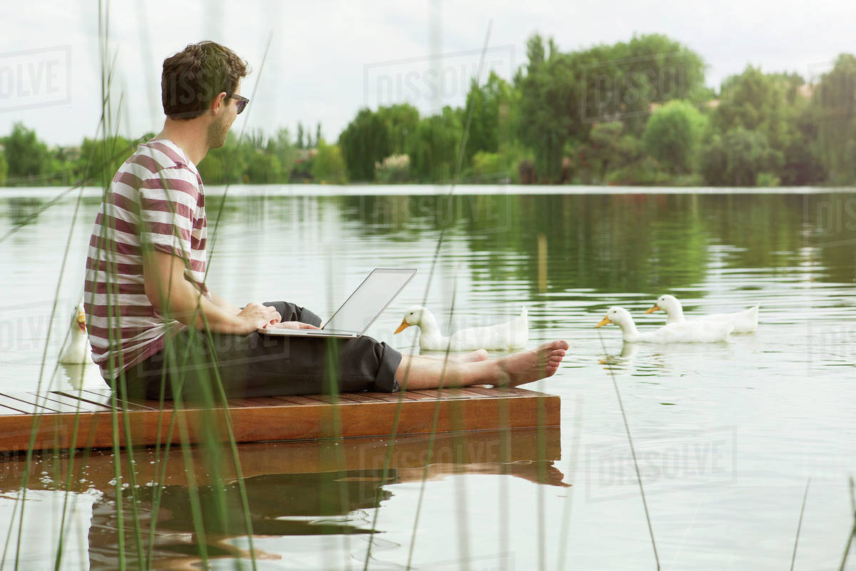 Man sitting on dock using laptop computer - Royalty-free Stock Photo ...