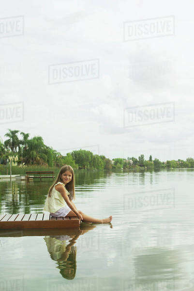 Girl sitting on dock with feet dangling in lake, portrait - Royalty ...
