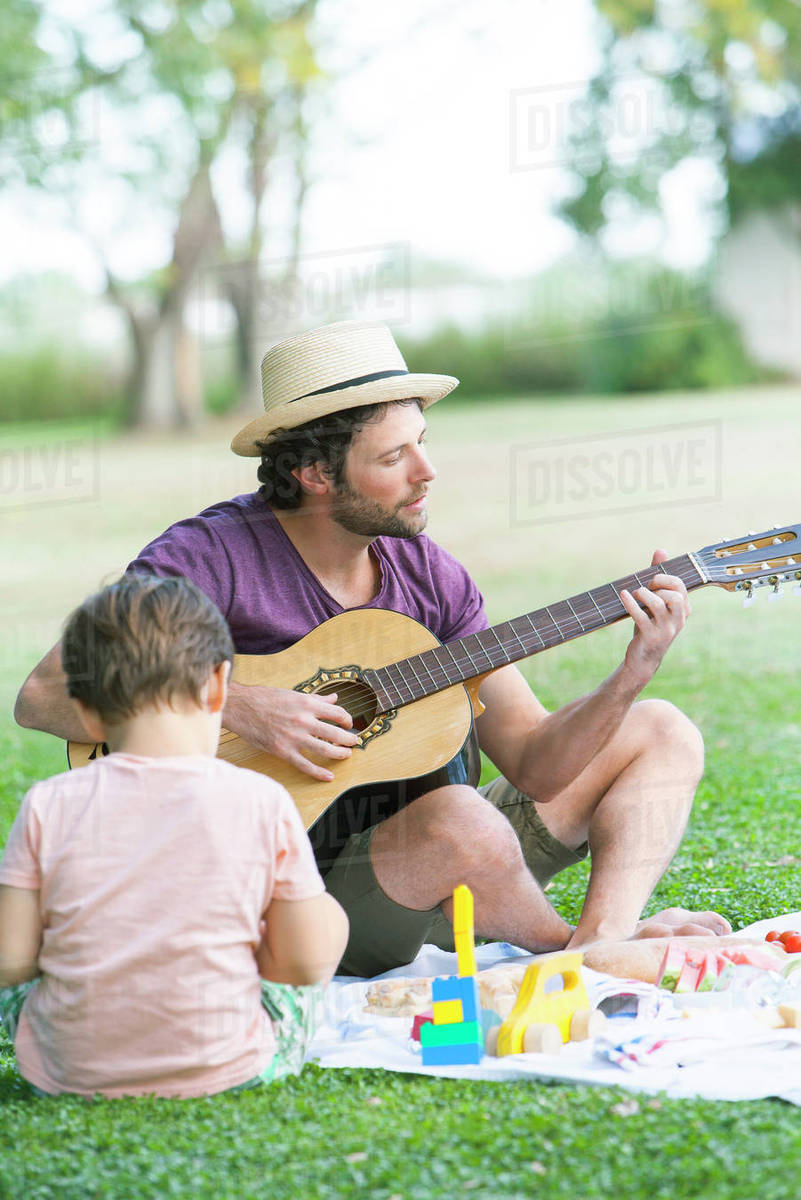 Father playing acoustic guitar next to son - Stock Photo - Dissolve