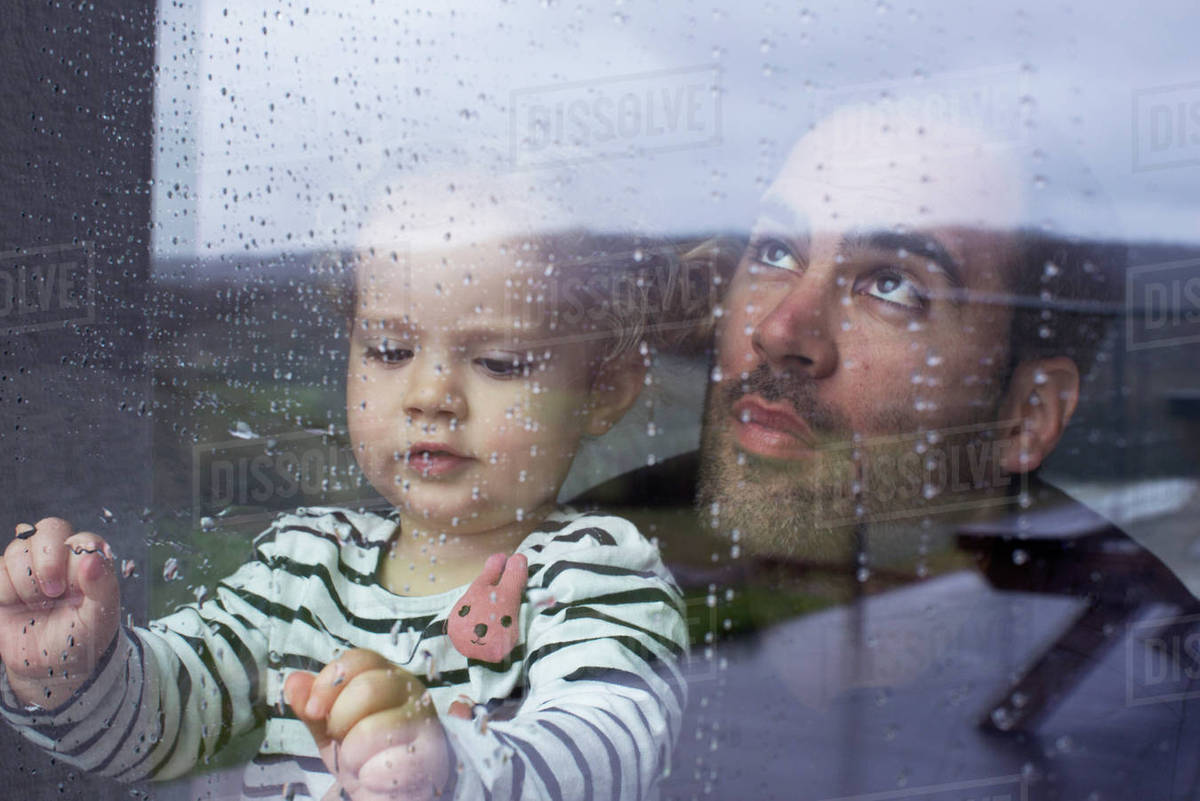 Man with young child looking through window watching rain fall - Stock ...