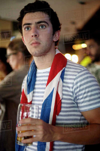 British football fan watching match in bar with flag draped around neck ...