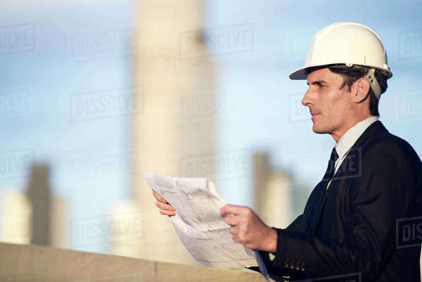 Man wearing hard hat outdoors reviewing blueprint - Stock Photo - Dissolve