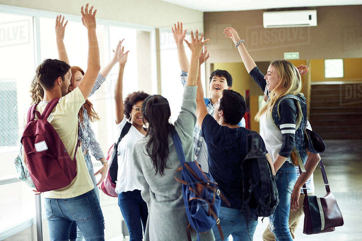 Group of students standing in a circle with hands raised in the air ...