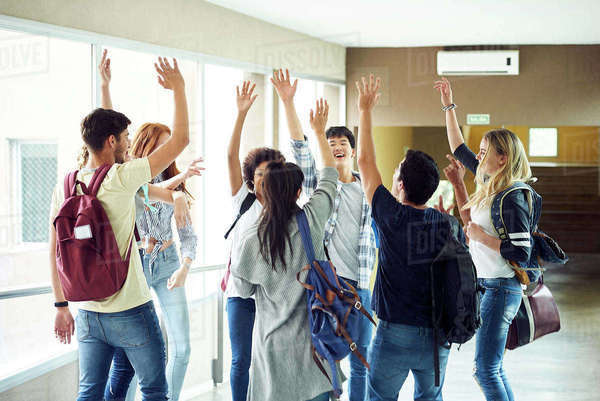 Group of students standing in circle in corridor with hands raised in ...