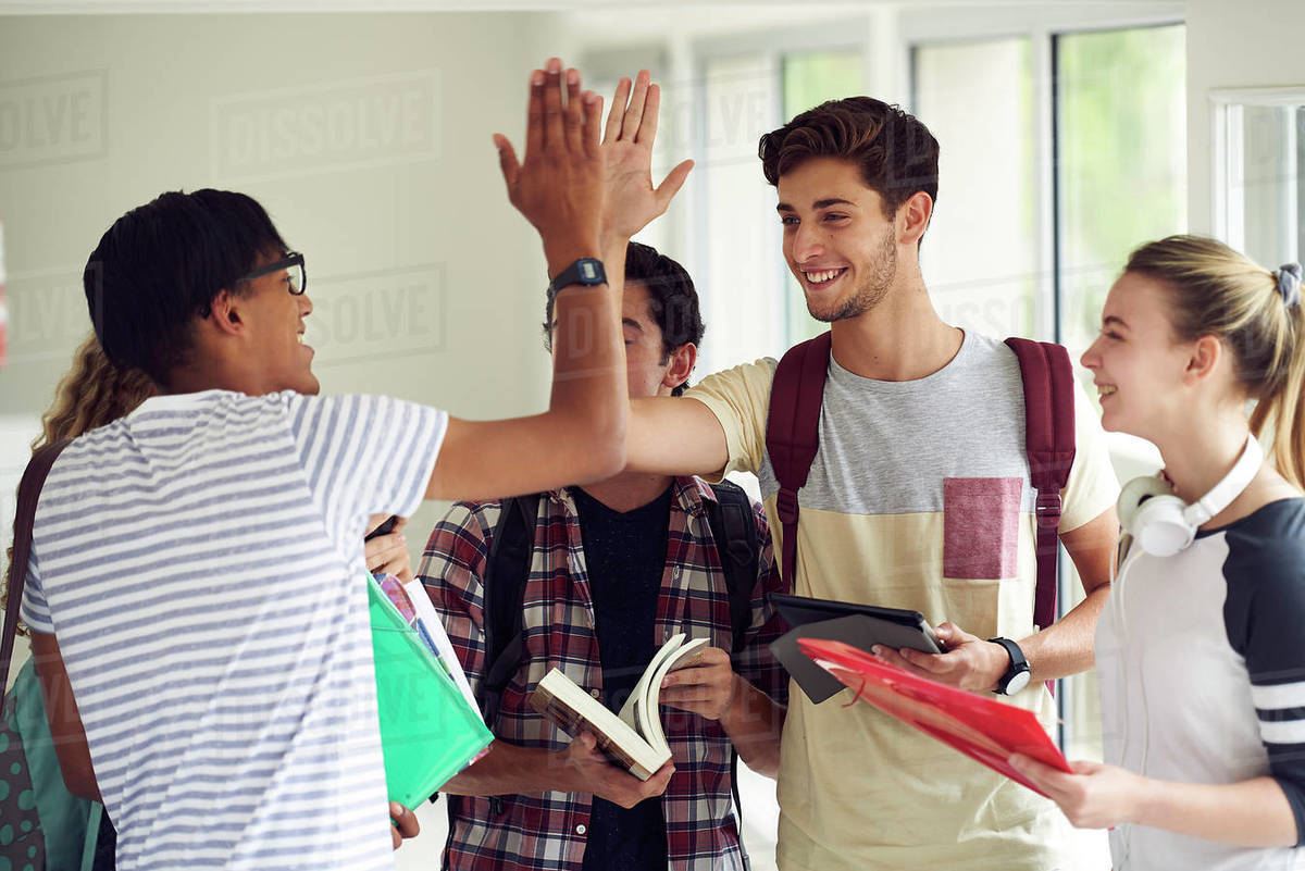 Students giving each other a high-five in corridor - Stock Photo - Dissolve