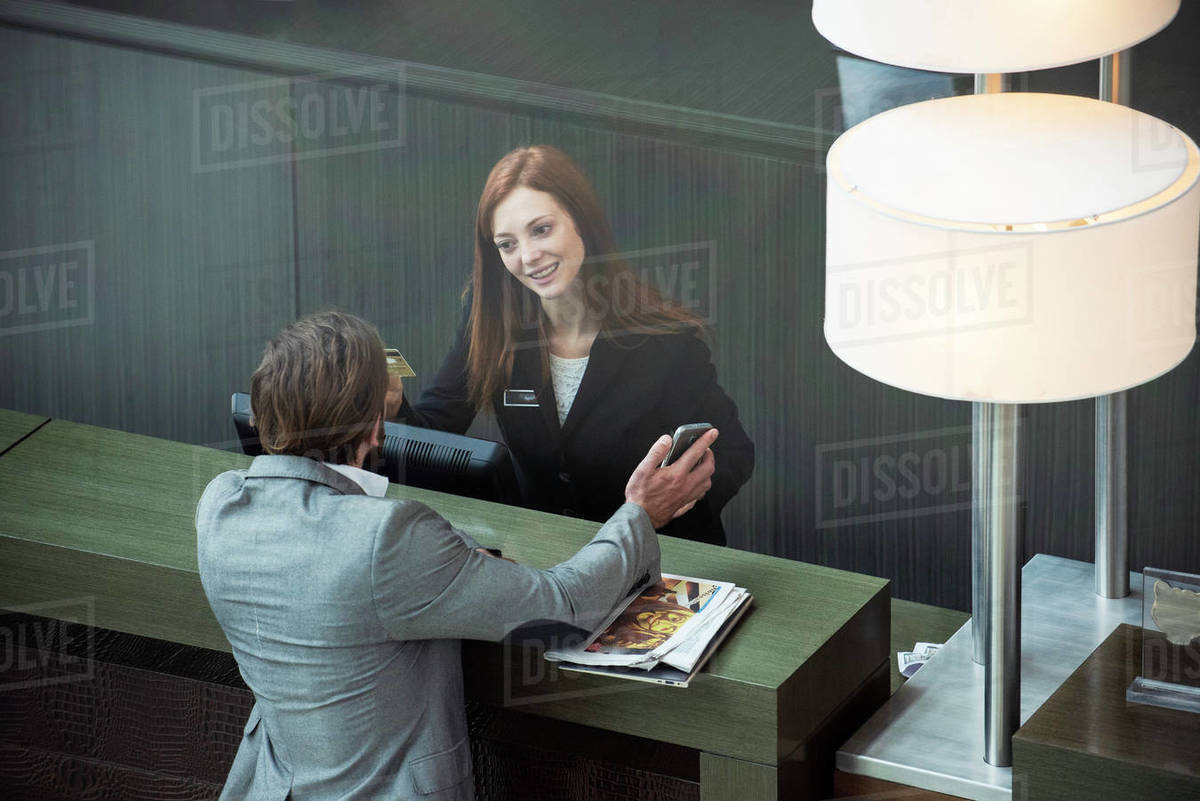 Businessman showing smart phone to female receptionist - Royalty-free ...