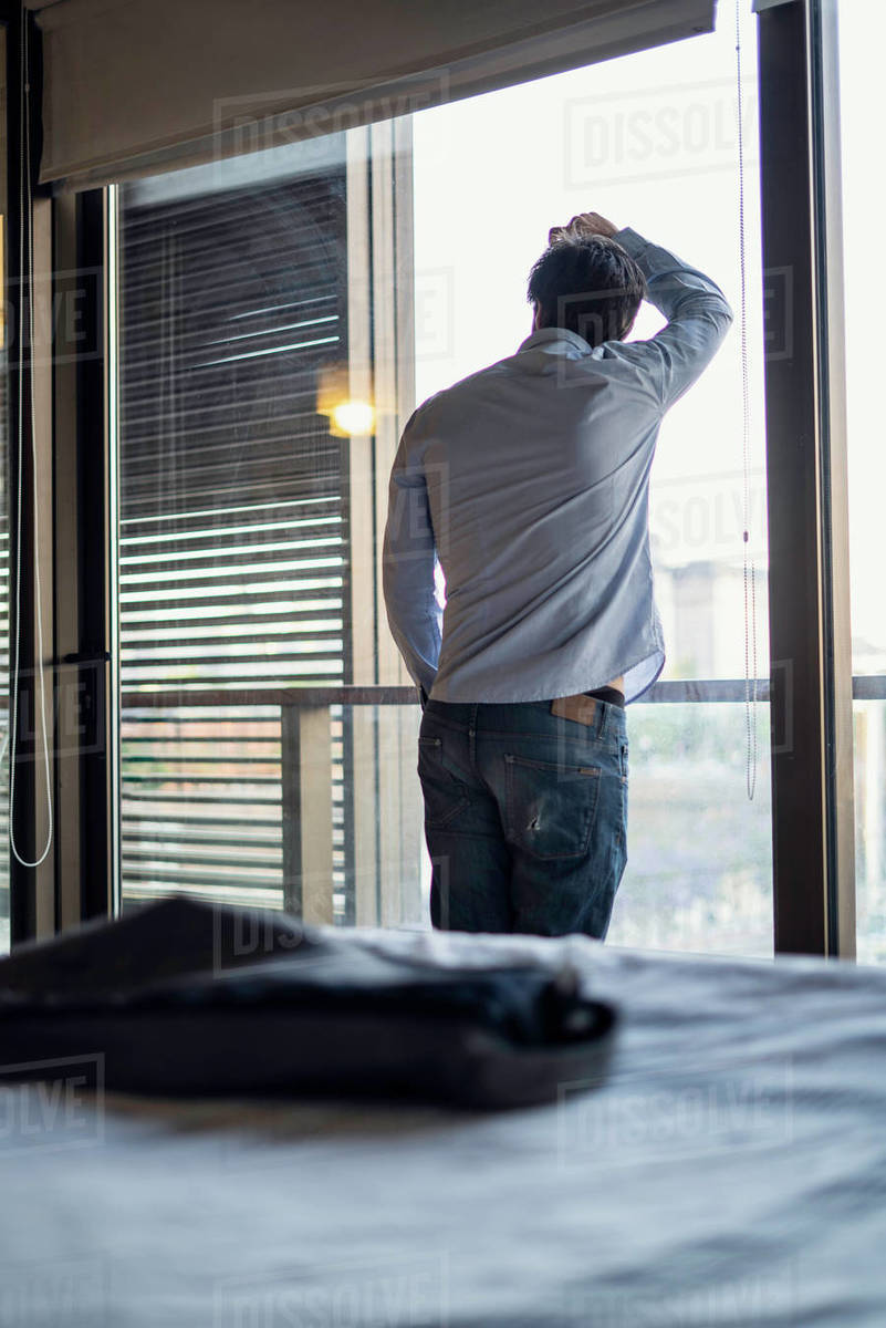 Thoughtful young man standing by the window - Stock Photo - Dissolve