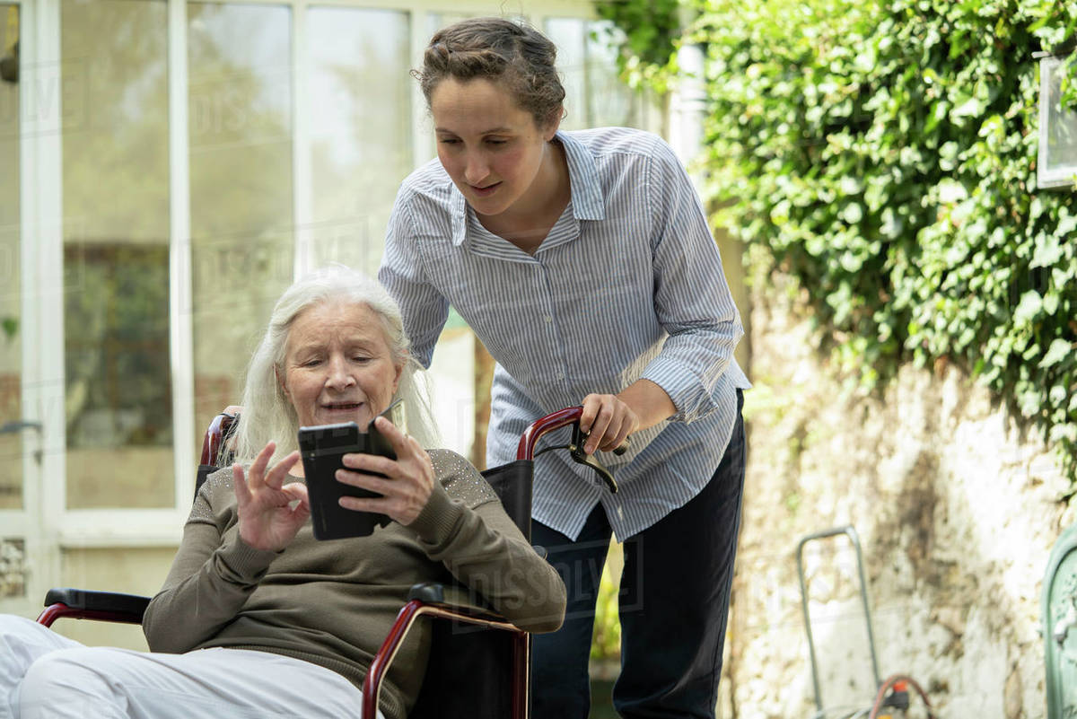 Senior female patient showing mobile phone to young home carer ...