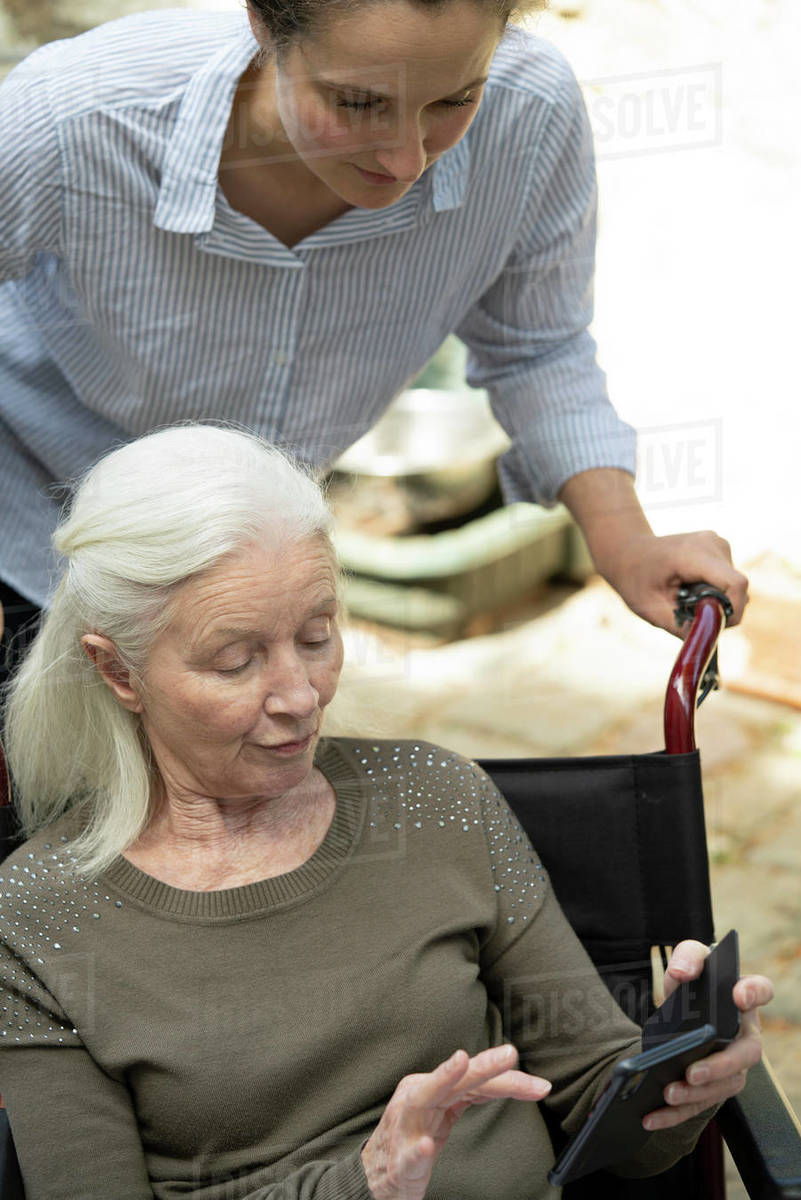 Senior female patient showing mobile phone to young home carer ...