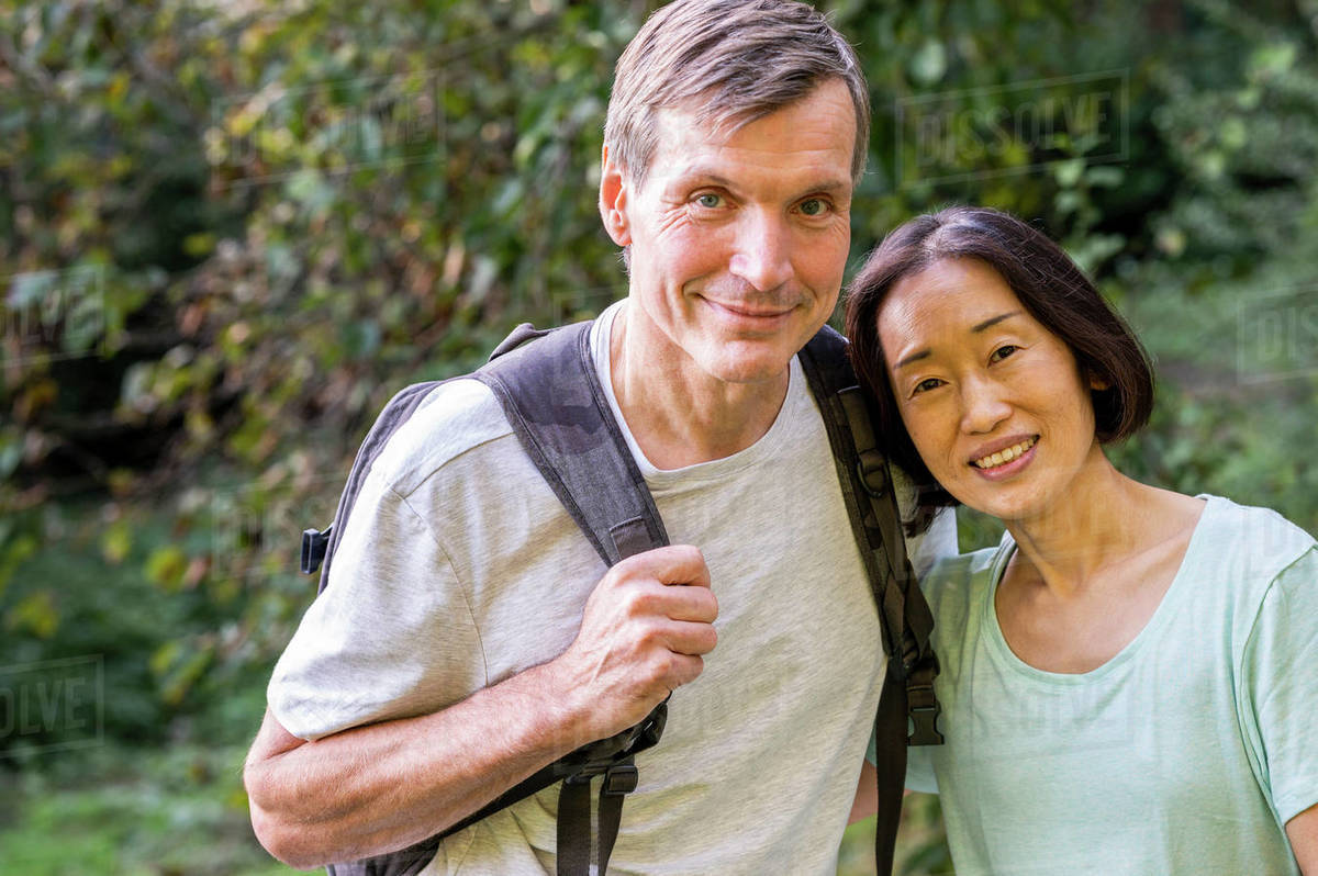Middle-aged diverse couple looking at camera while hiking out in the ...