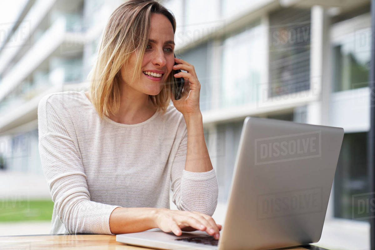 Mid-shot portrait of woman working outdoors on laptop computer while ...