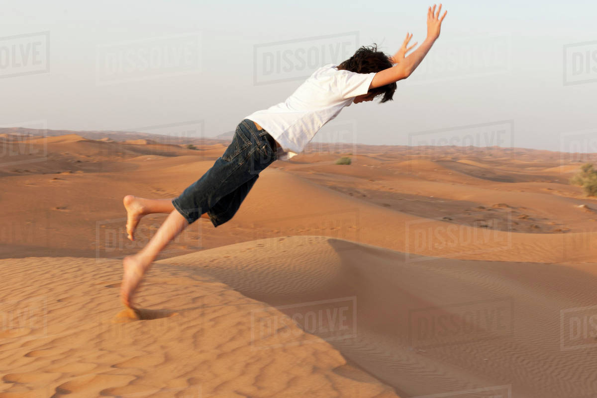 Teenage boy pretending to fall from top of desert sand dune - Royalty ...