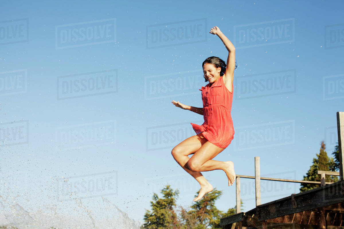 Smiling woman jumping off dock - Royalty-free Stock Photo | Dissolve